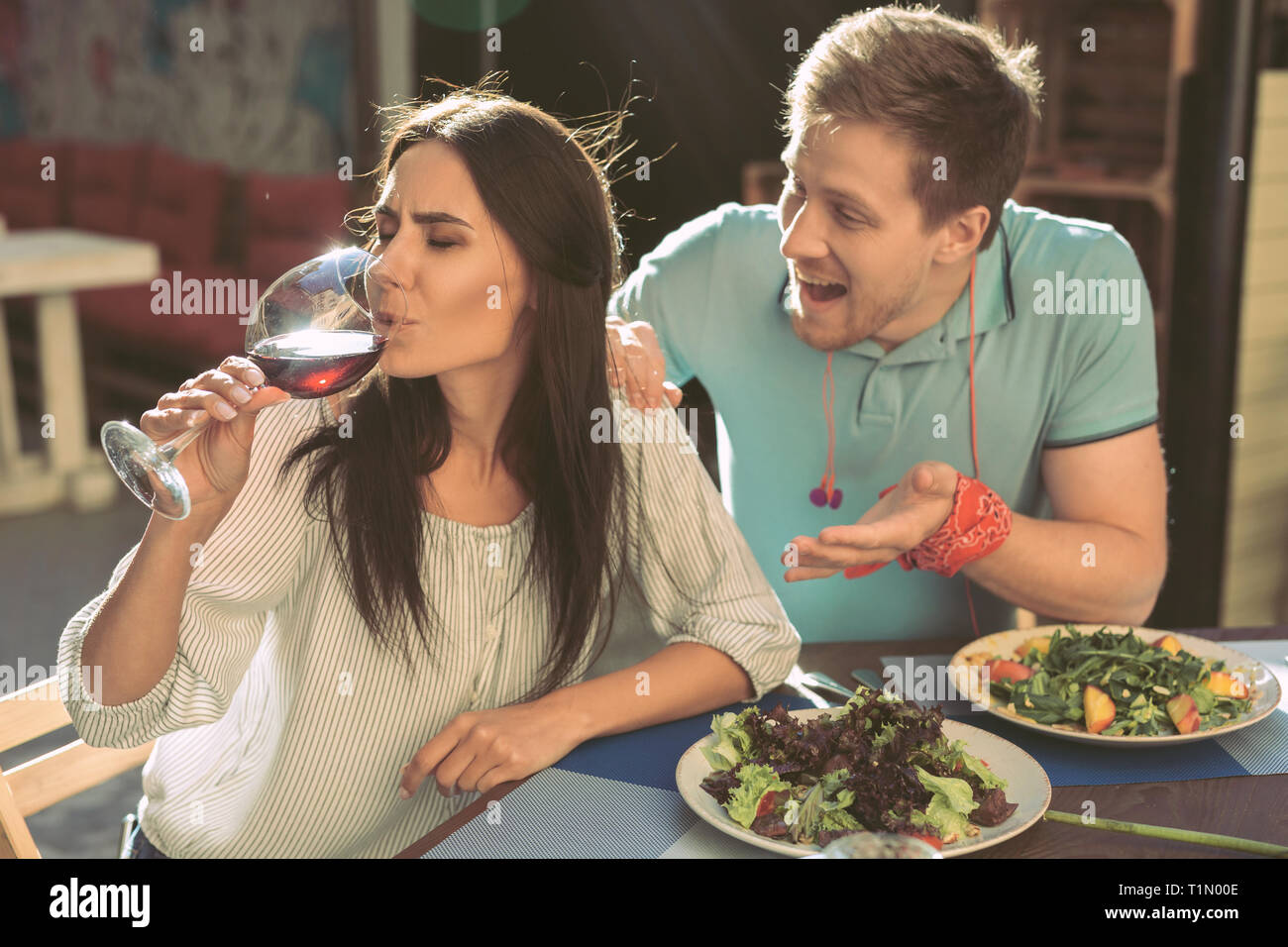 Resolute dark-haired girl drinking wine from glass while her boyfriend ...