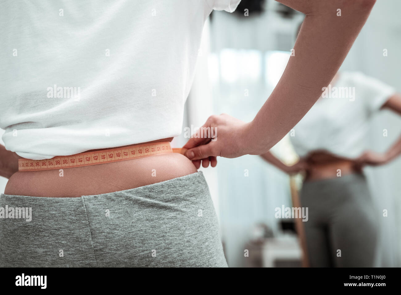 Young woman measuring a waist near the mirror Stock Photo - Alamy