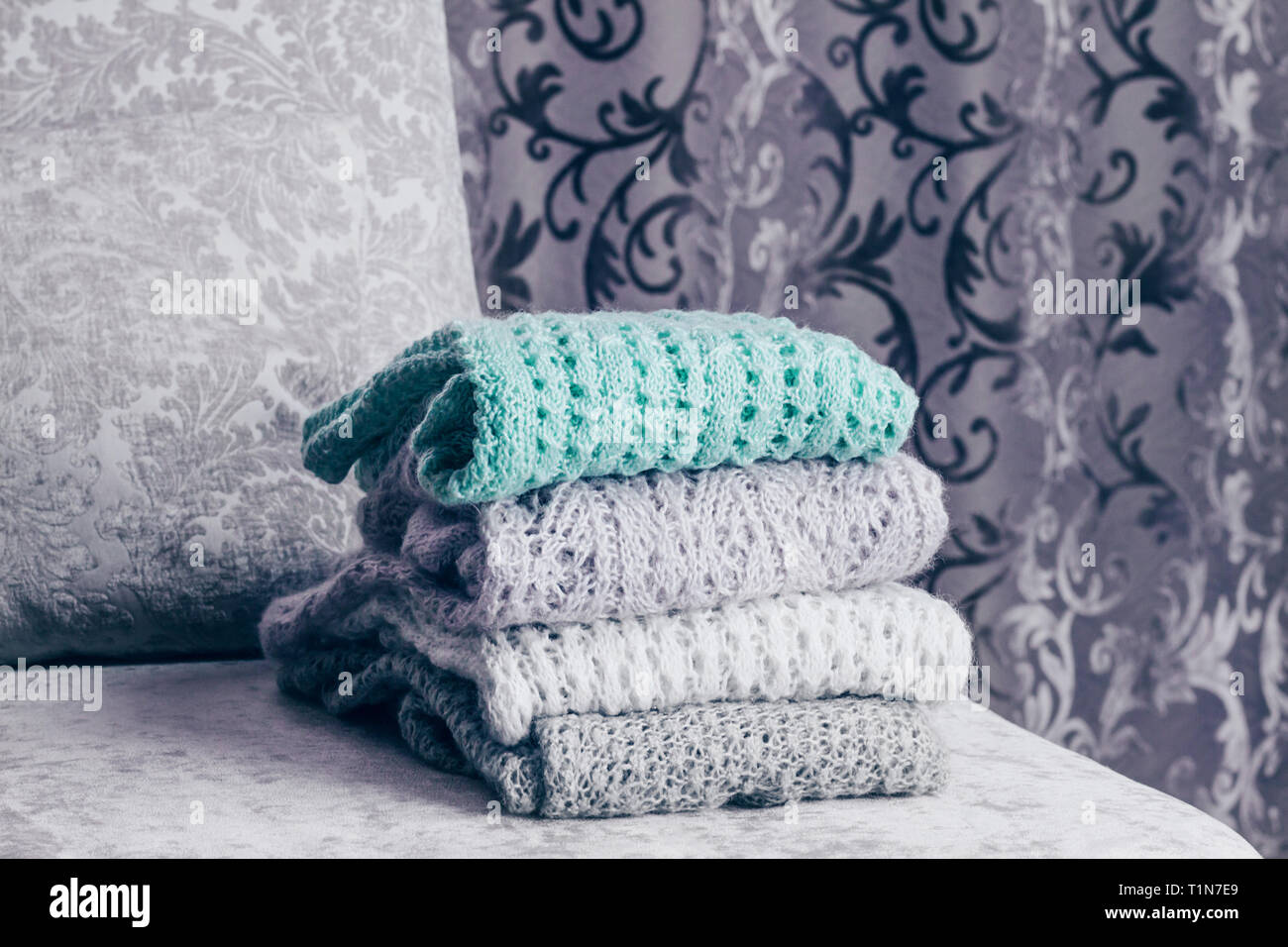 Stylish knitted pastel colored sweaters folded in stack on velvety ...