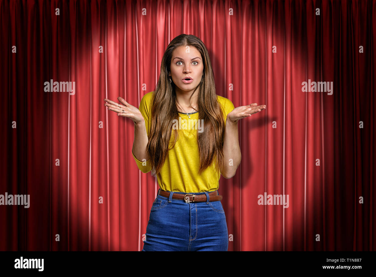 Young amazed, surprised girl wearing jeans and yellow shirt on red ...