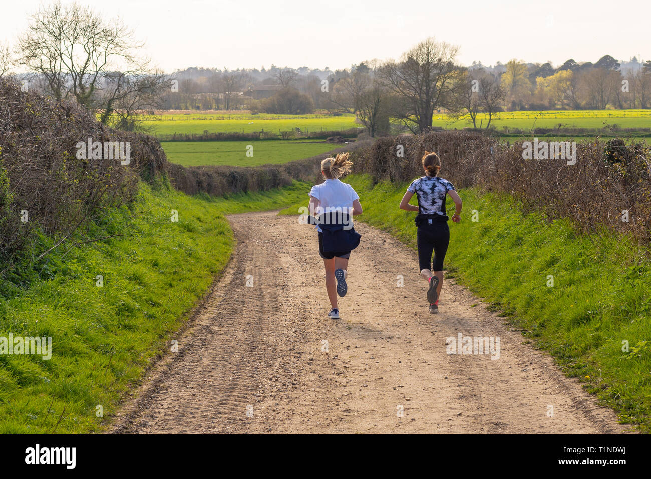 Two women running along a countryside track in bright spring sunshine ...