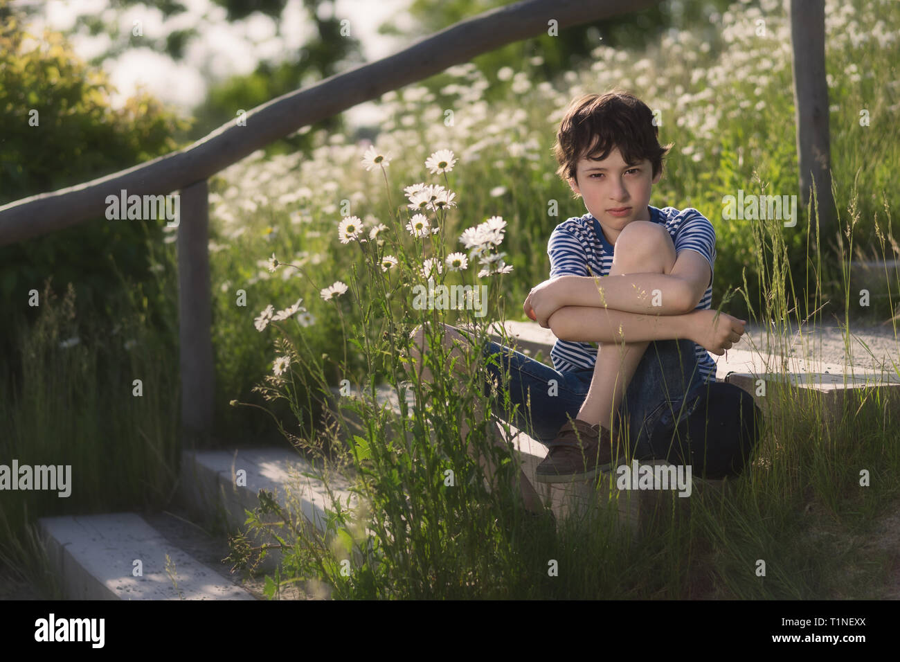 Portrait of a boy sitting on the steps in the park. In the background ...