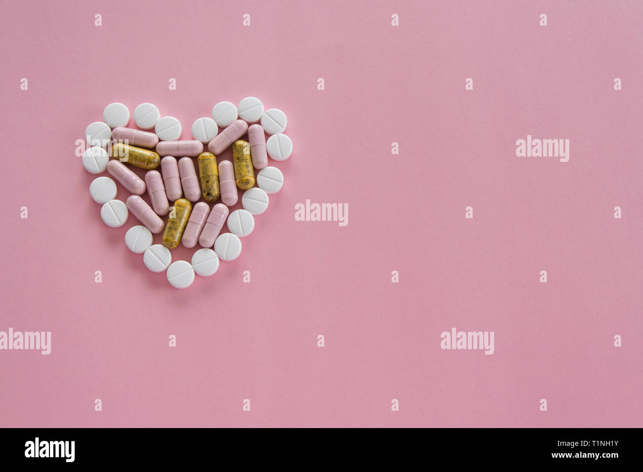 Different medication pills in heart shape on pink background ...