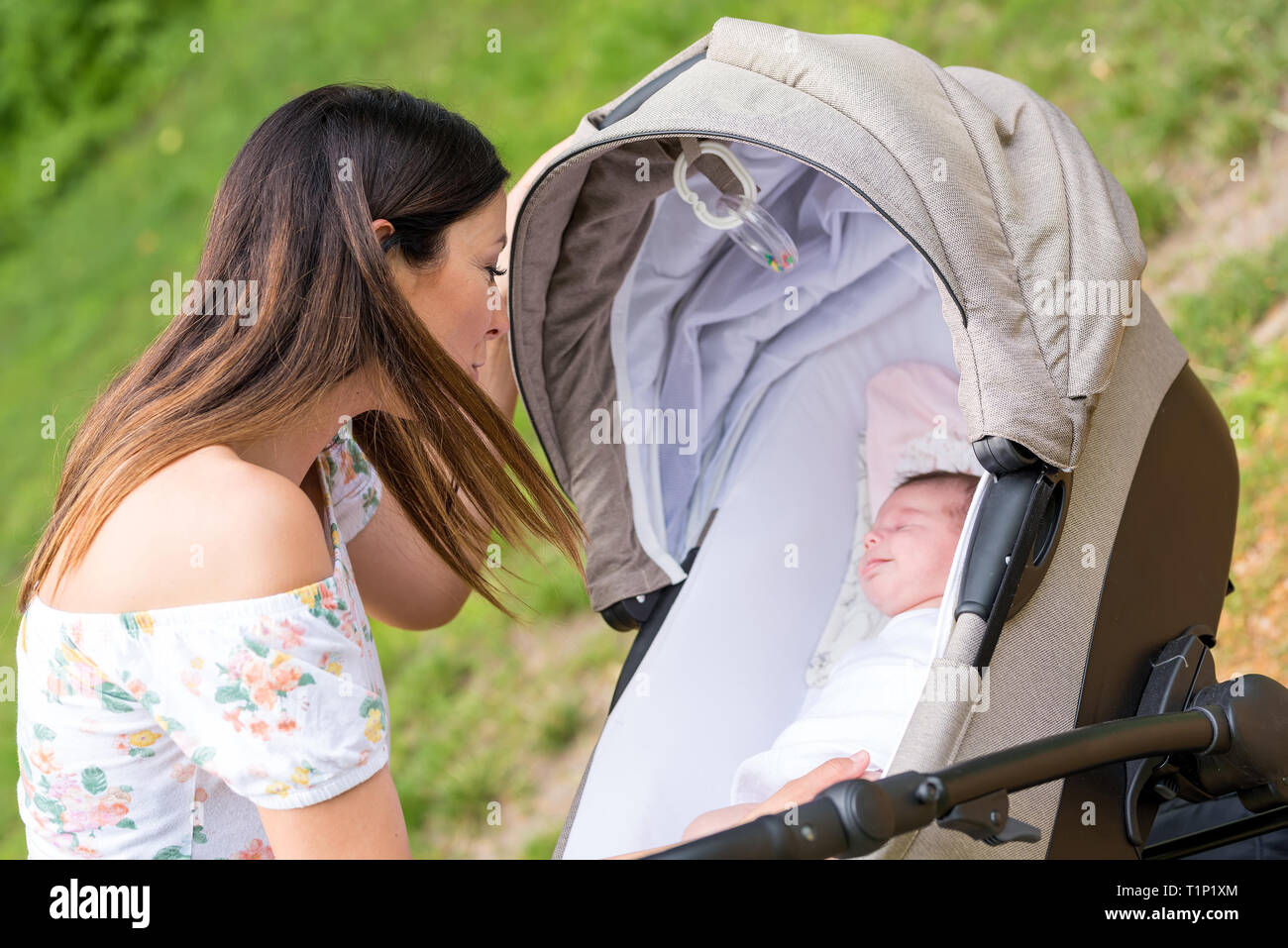 A beautiful mother checking her baby in a stroller in the park on a ...
