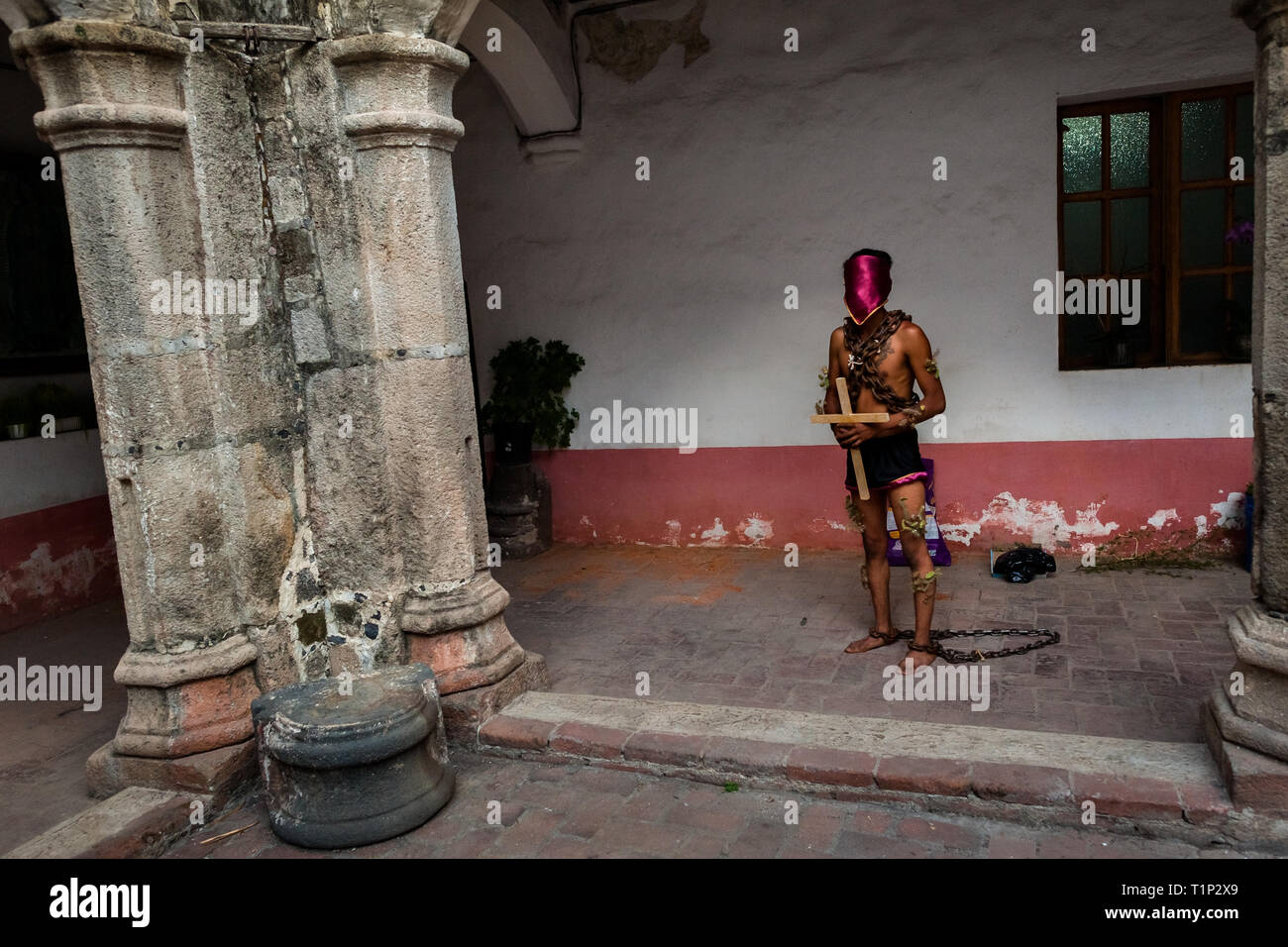 A chained Catholic penitent, holding a wooden cross, prepares to ...