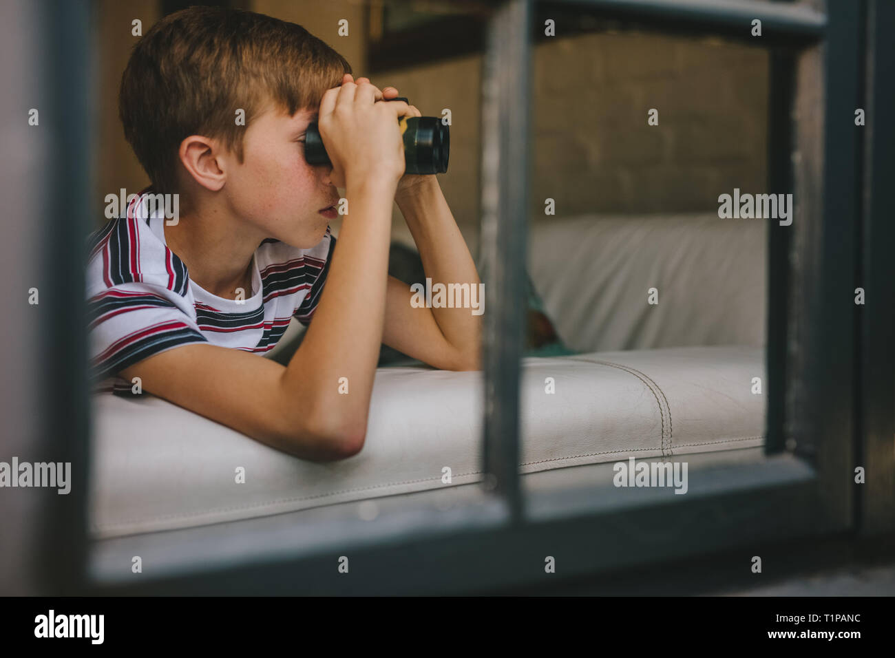 Curious boy looking out the window with binocular. Small boy on sofa ...