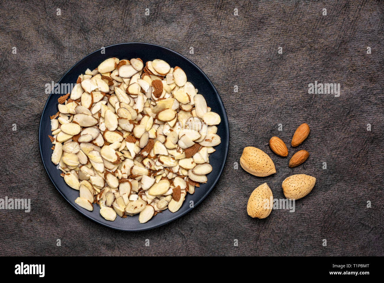 almond slices and on a black plate against textured bark paper with a ...