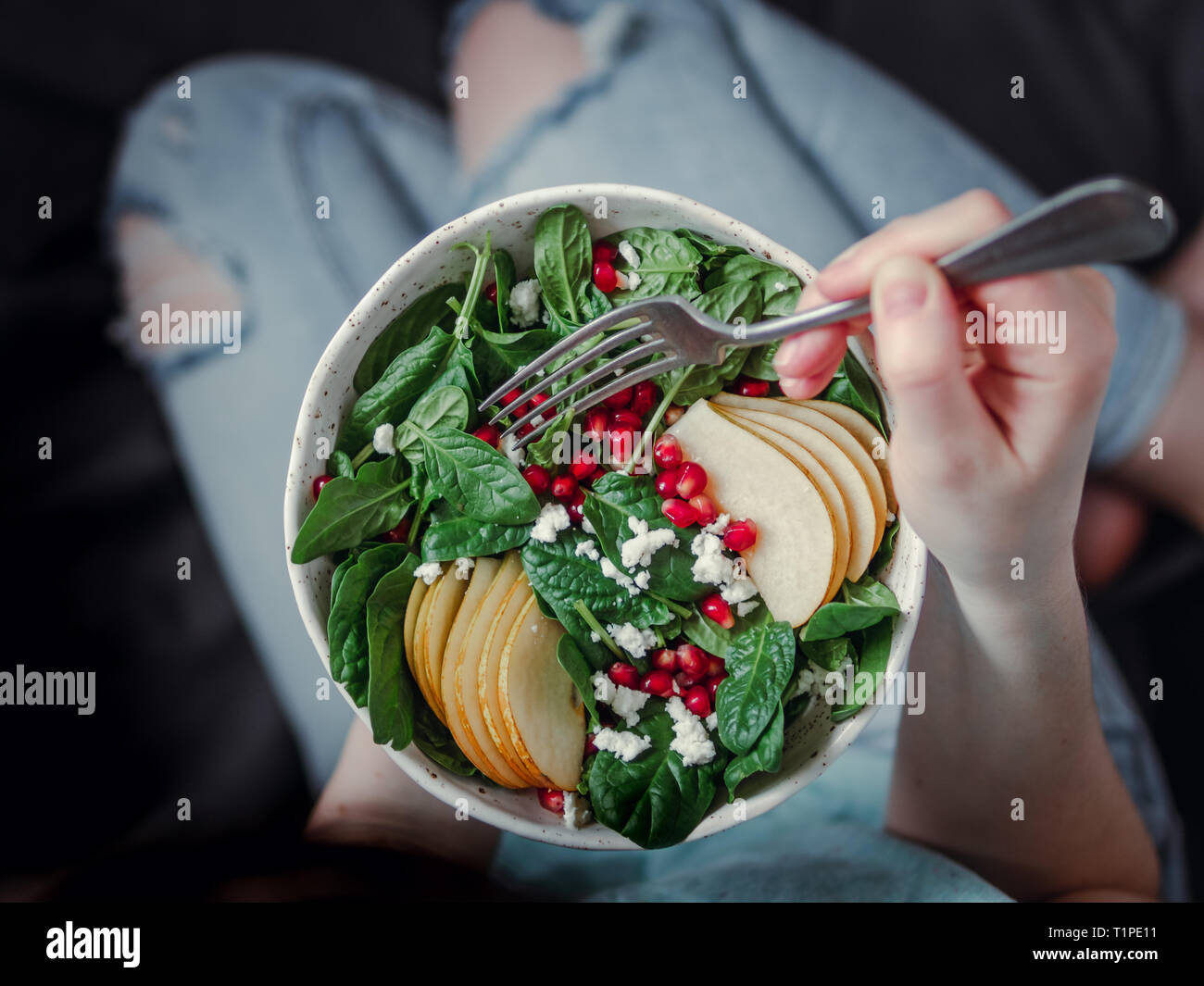 Woman in jeans holding vegan salad bowl with spinach, pear, pomegranate ...
