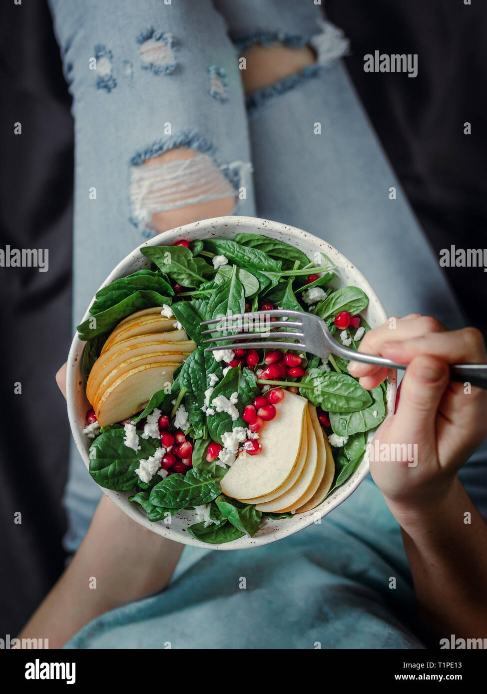 Woman in jeans holding vegan salad bowl with spinach, pear, pomegranate ...