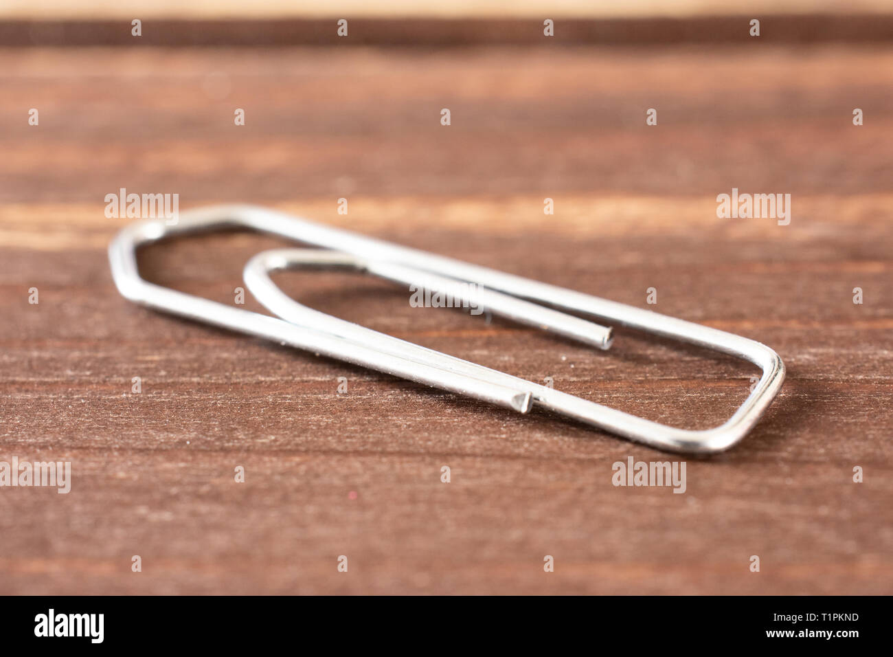 Closeup of metal paper clip on brown wood Stock Photo - Alamy