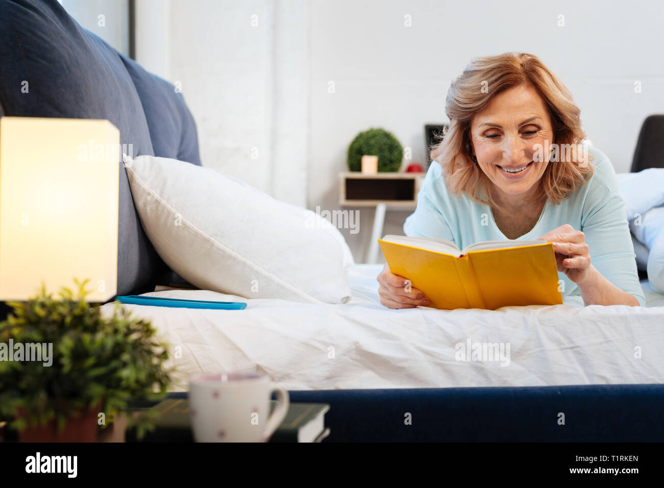 Beaming appealing mature woman being interested in book Stock Photo - Alamy