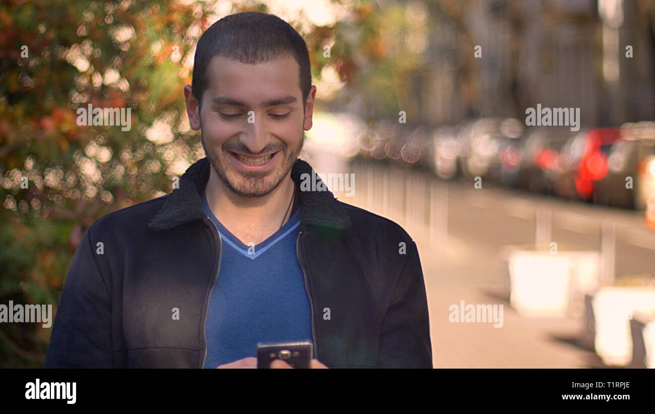 Portrait of caucasian man watching joyfully into smartphone on sunny ...