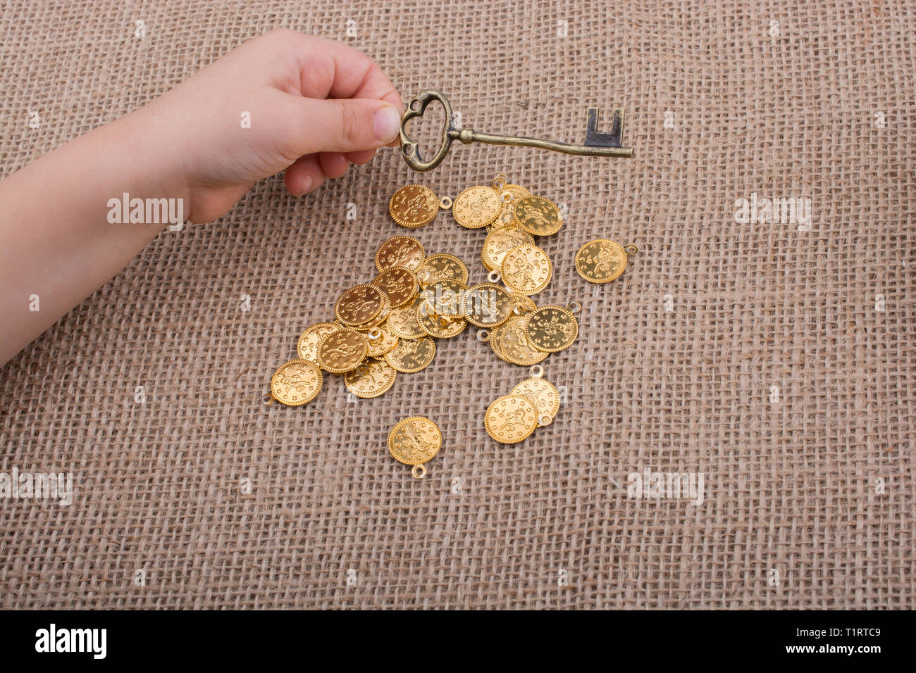 Hand holding a retro styled key over fake gold coins Stock Photo - Alamy