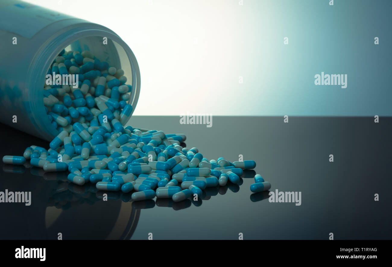 Blue and white capsule pill spilled out from white plastic bottle ...