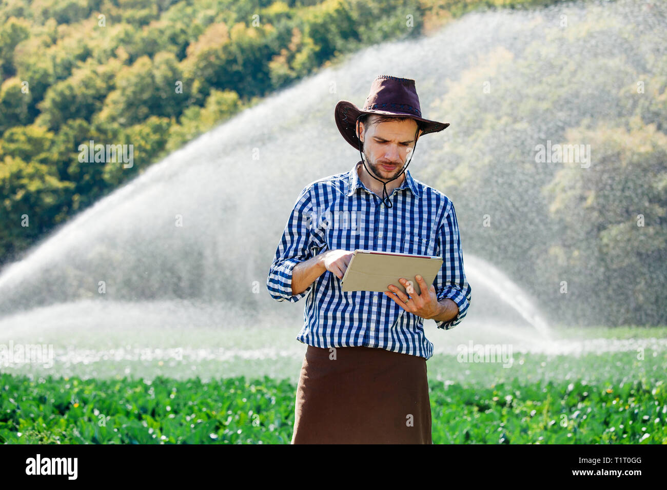 Farmer using digital tablet computer on sprinkler system background. A ...