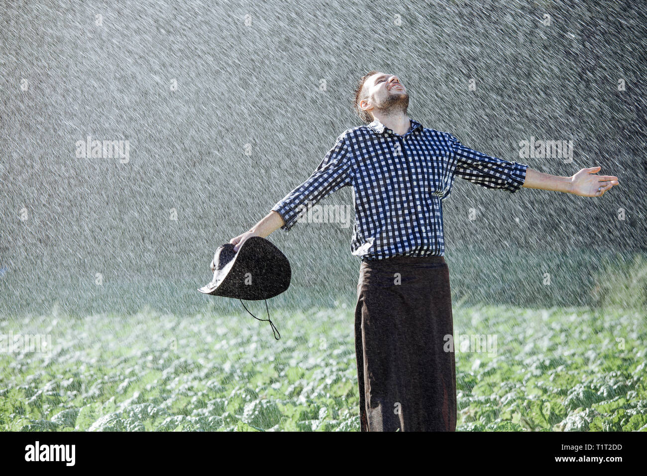 The farmer in the hat is enjoying the rain. Young man getting wet under ...