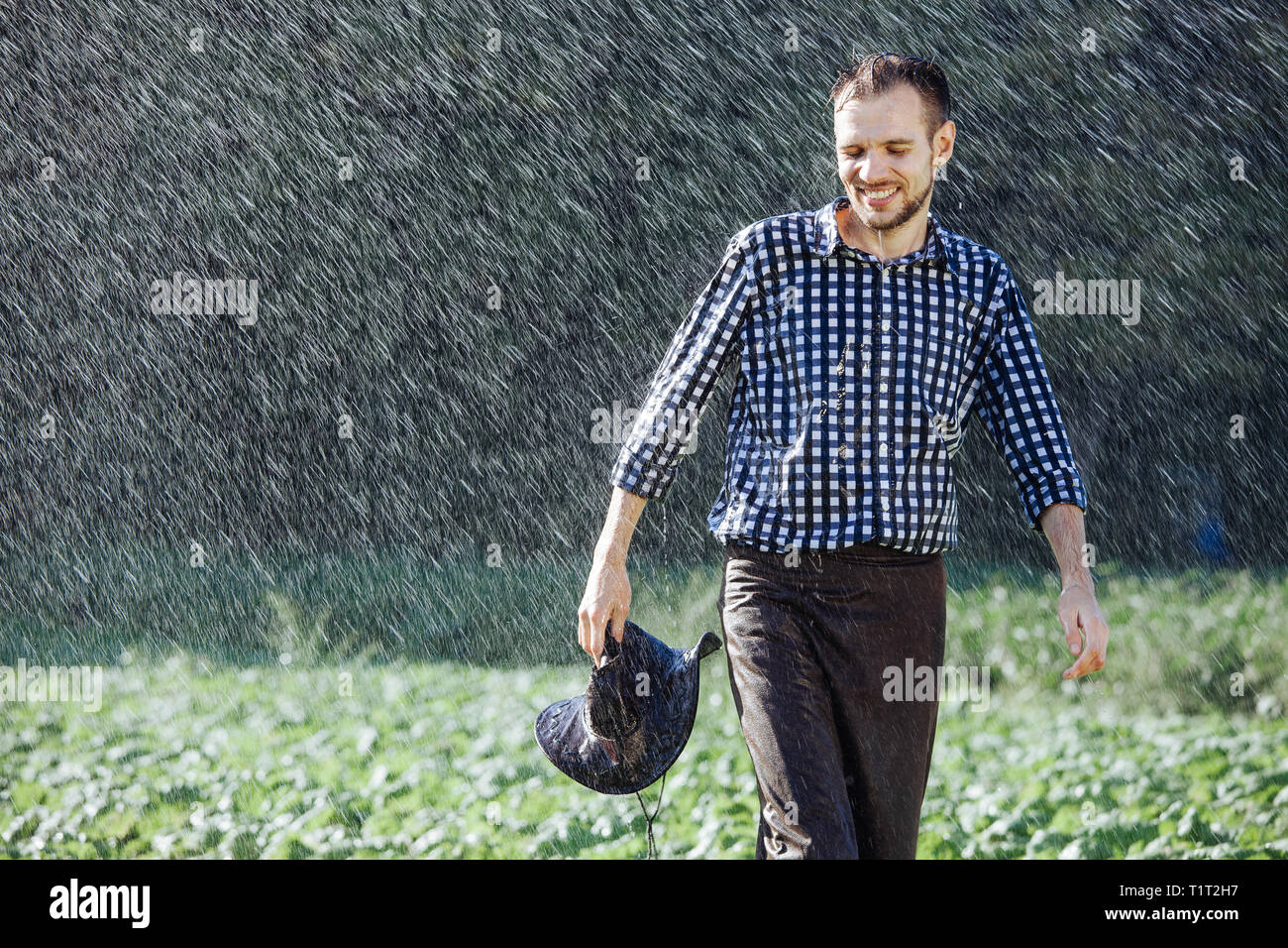 The farmer in the hat is enjoying the rain. Young man getting wet under ...