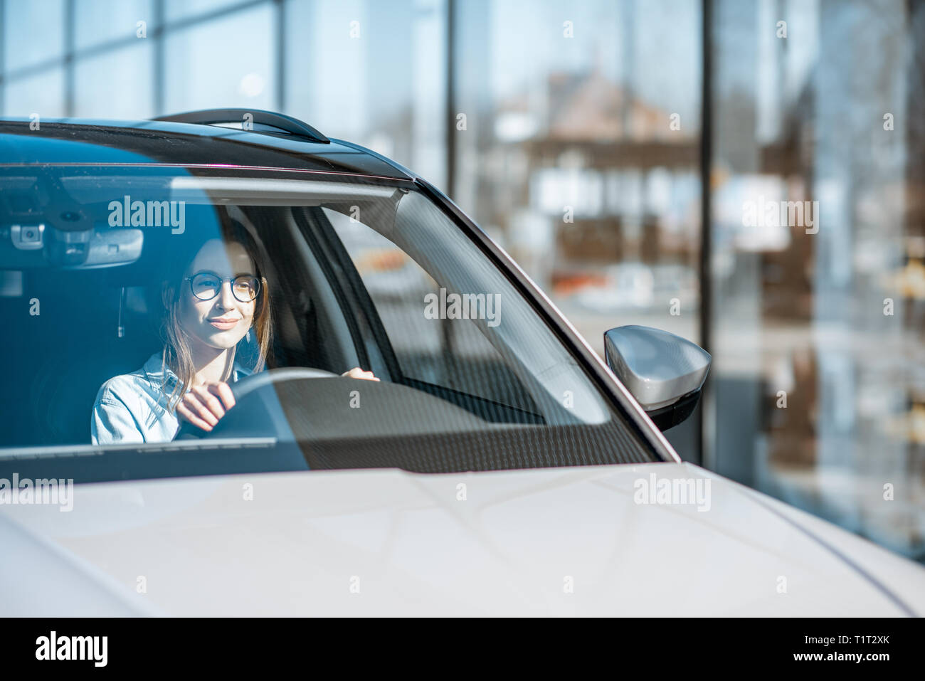 Young and happy woman driving a luxury car in the city, front view ...