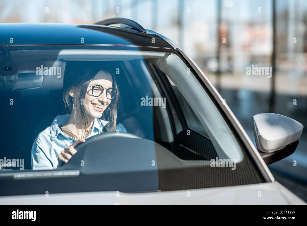 Young and happy woman driving a luxury car, front view through the ...