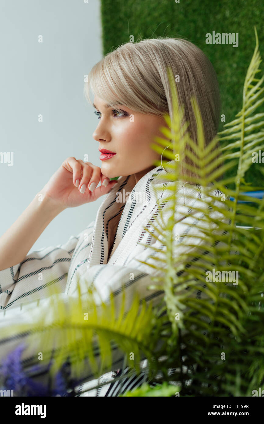 side view of beautiful stylish blonde girl posing near fern leaves ...