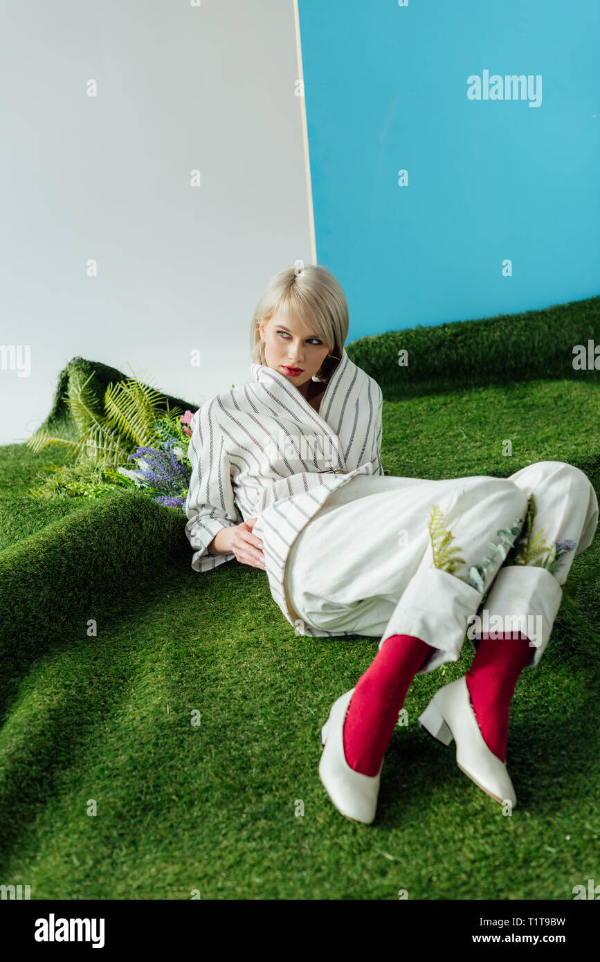 beautiful stylish blonde girl posing on artificial grass with fern and ...