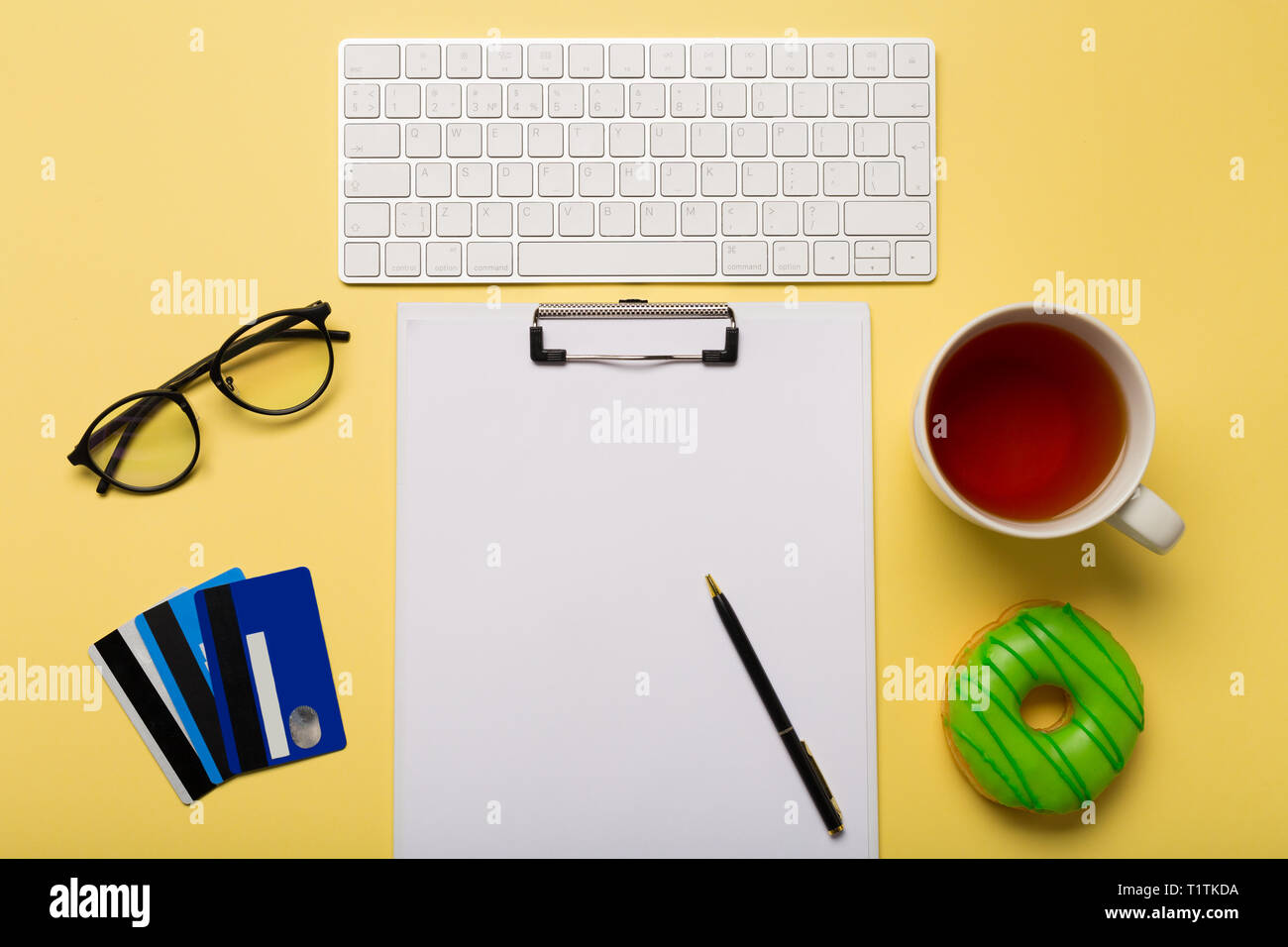 Keyboard, cup of tea, credit cards, paper and pen on yellow background ...