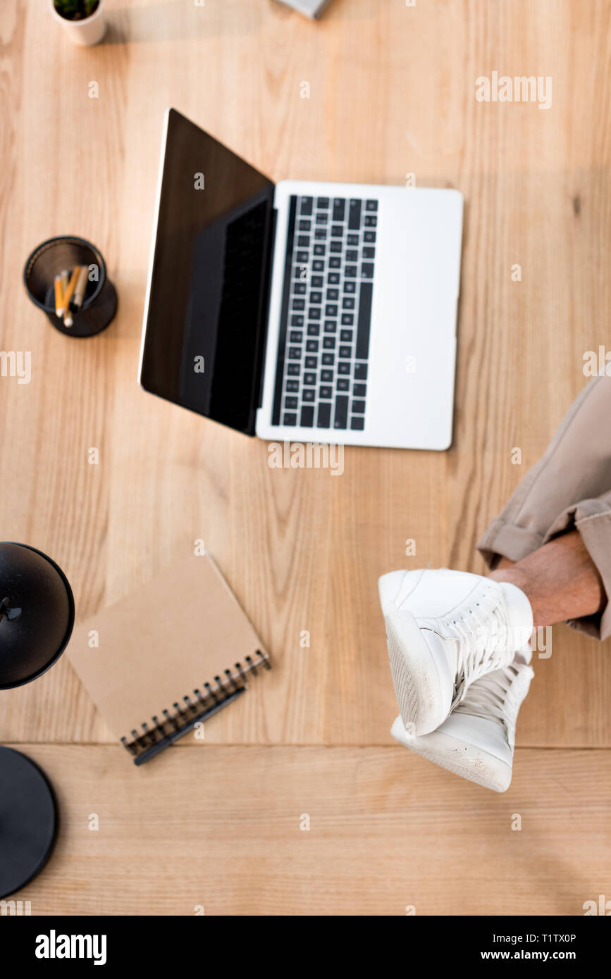 top view of laptop with blank screen with male legs in white sneakers ...