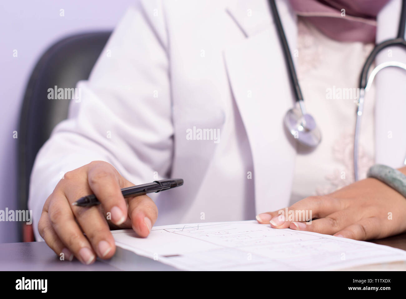 hijab female doctor hand writing on a paper for receipt on her desk ...