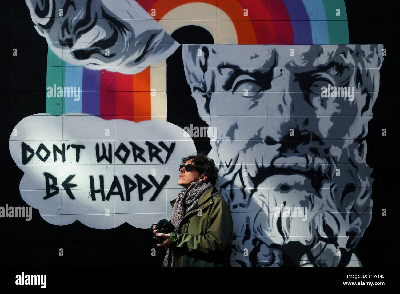 A tourist enjoys the sunshine as he leans against a new mural by art ...