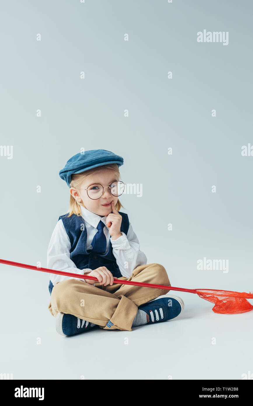 thoughtful kid sitting with crossed legs and holding red butterfly net ...