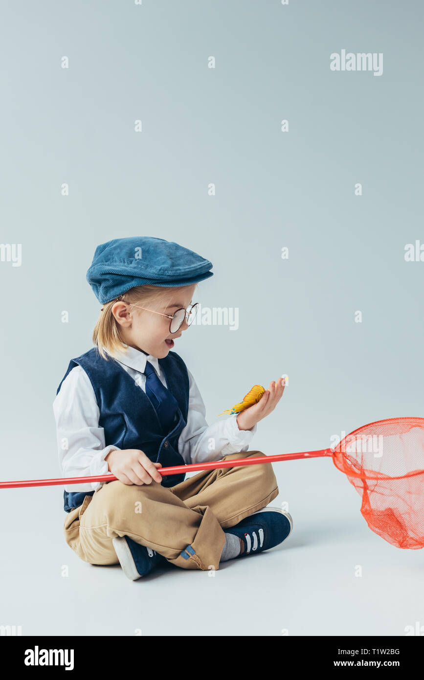 surprised kid sitting with crossed legs and holding red butterfly net ...