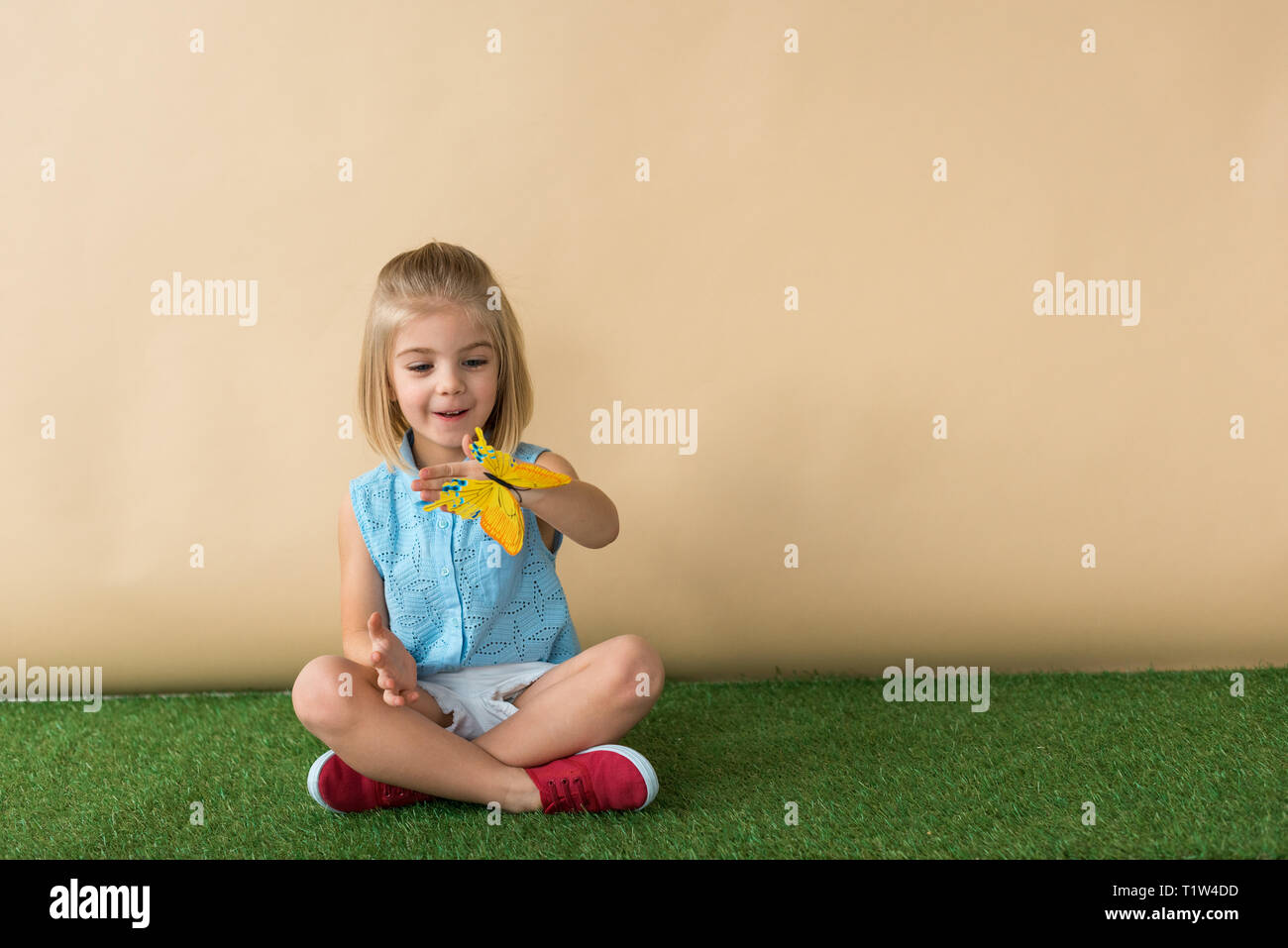happy and cute child sitting with crossed legs and holding butterfly ...