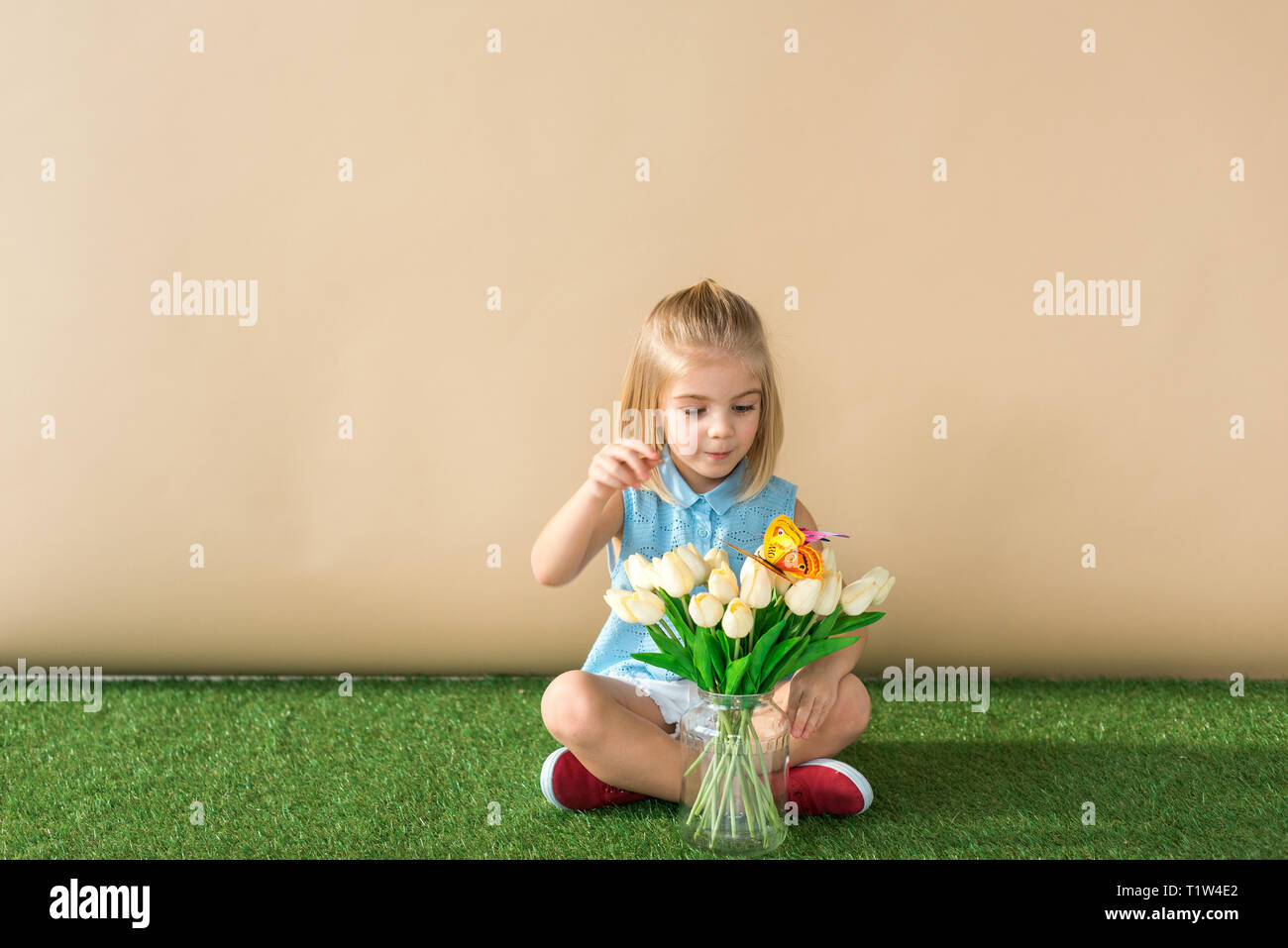 child sitting with crossed legs, looking at flowers and catching ...