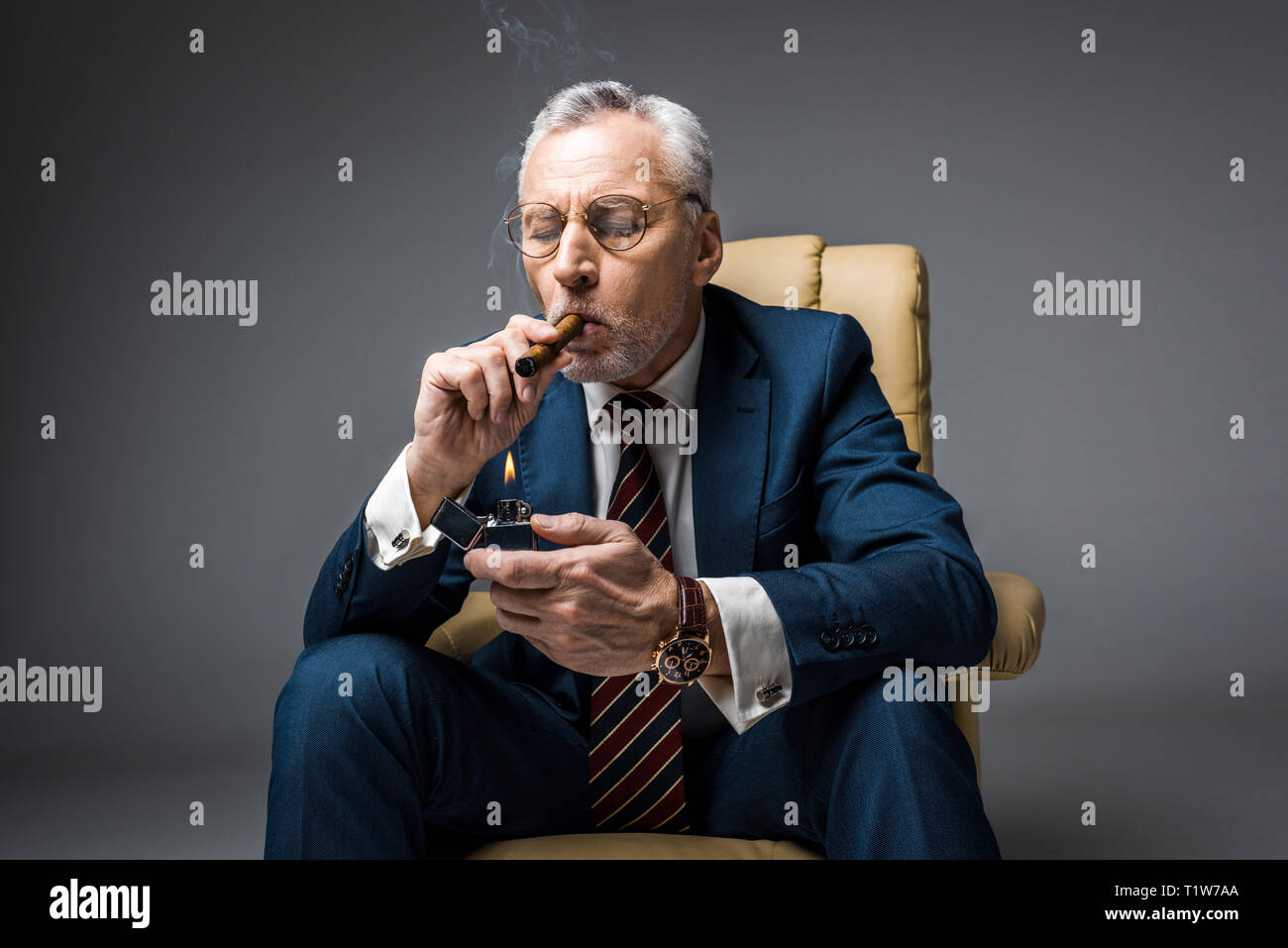 mature man in suit holding lighter while smoking cigar with closed eyes ...