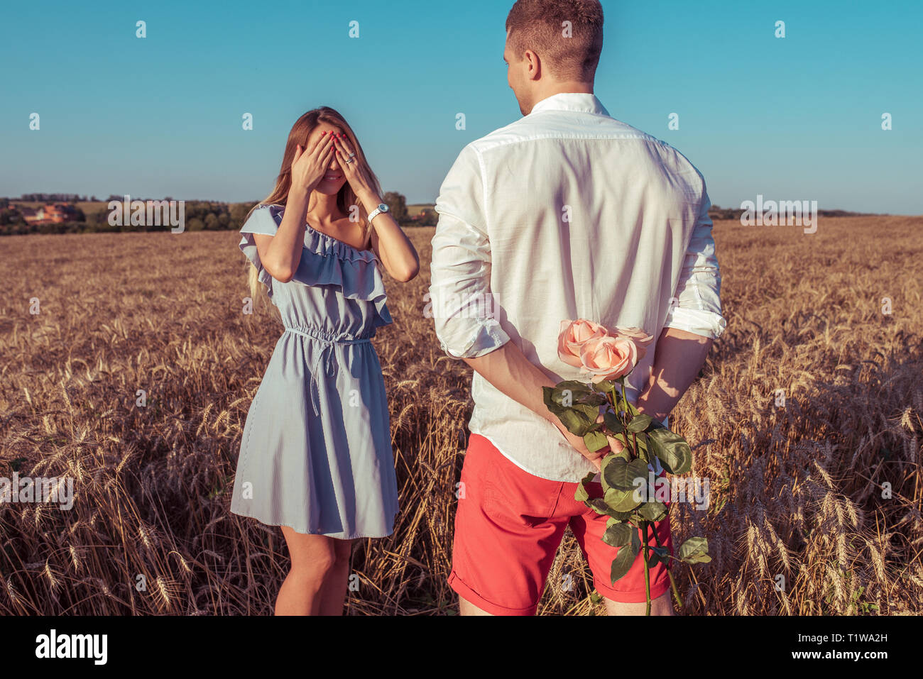A man gives a gift to girl behind his back holds a bouquet of flowers ...