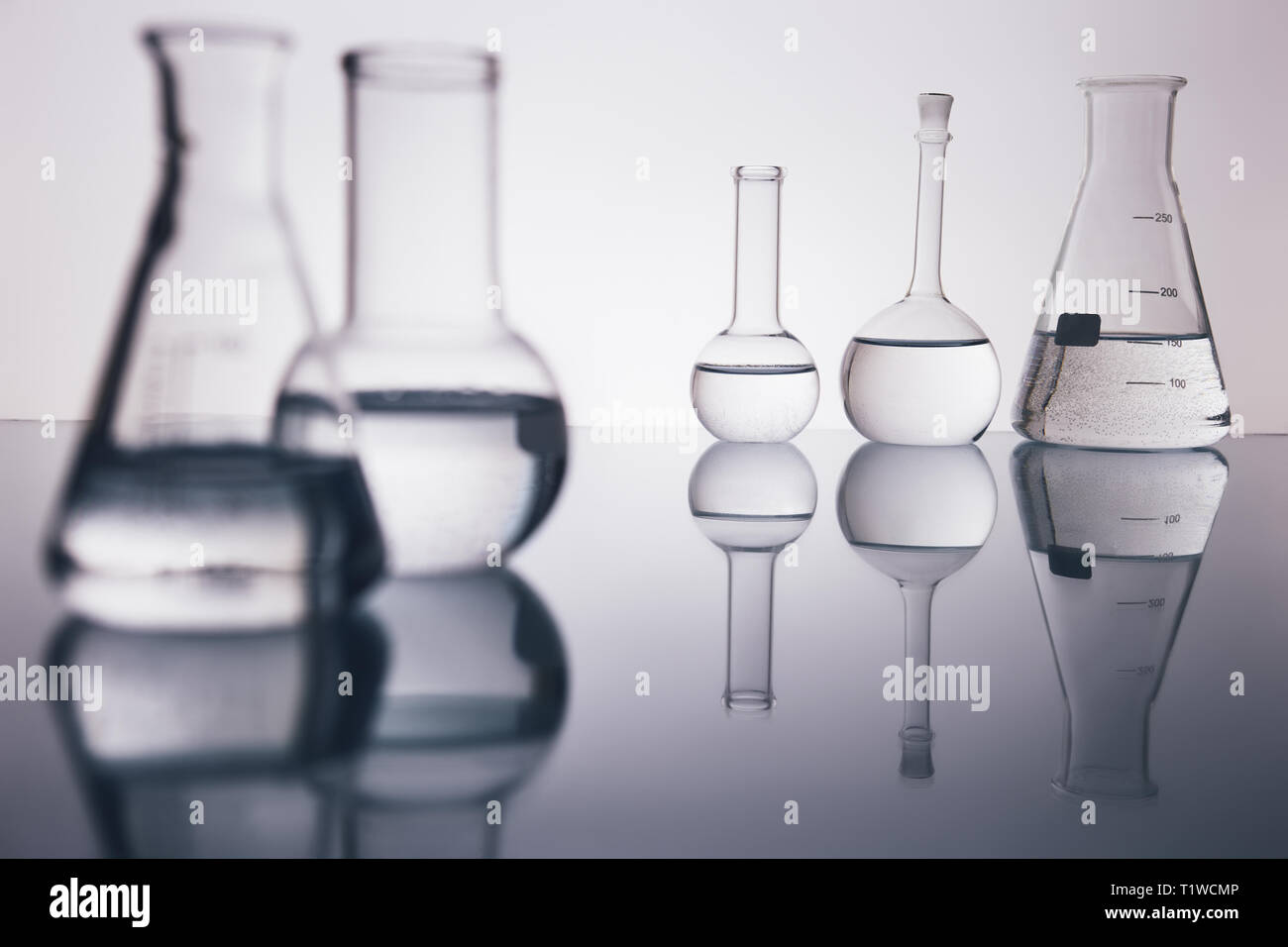 many beakers are in row, with liquid, in backlight, reflection, blue ...