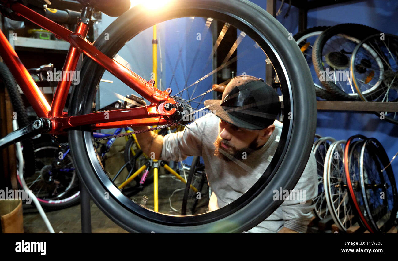 A man bike mechanic with a beard assembles a mountain bike in his ...
