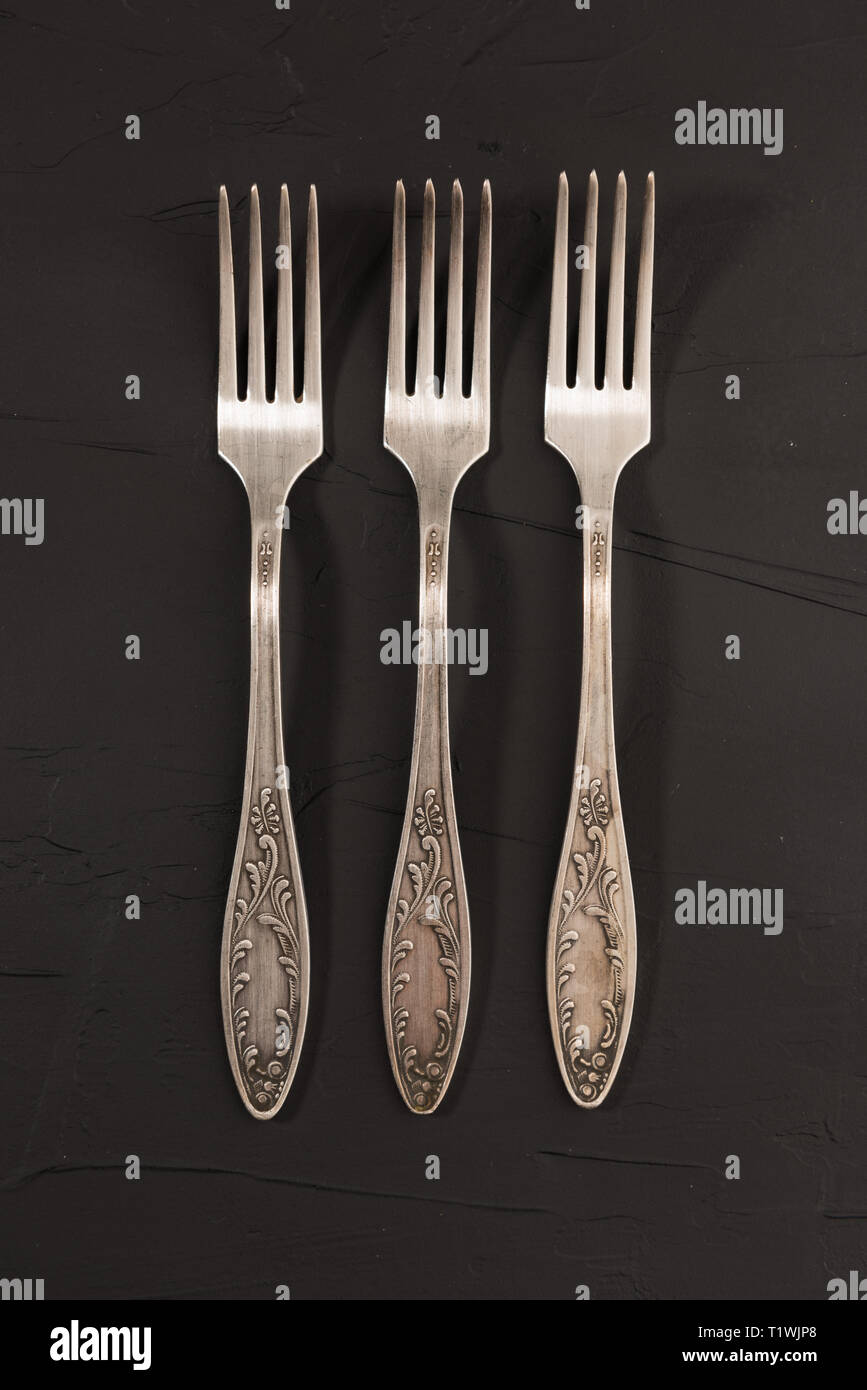 Very old set of three rusty vintage silver forks on a black cement ...