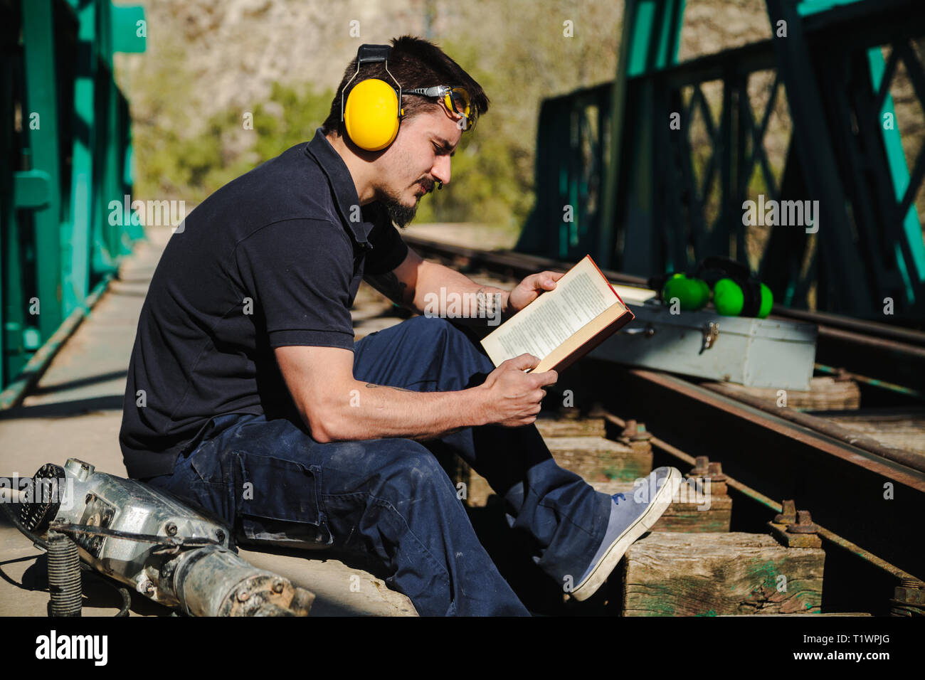 Young construction worker man sitting reading a book on an old steel ...