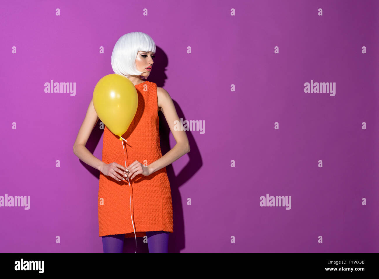 Girl in white wig holding yellow air balloon on purple background Stock ...