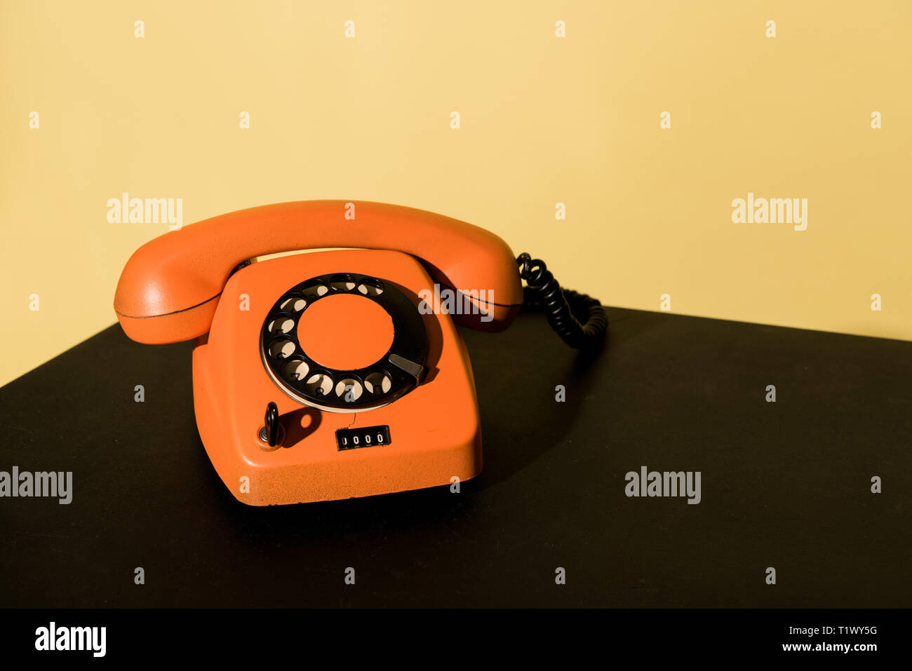 Old orange telephone standing on black surface on yellow background ...