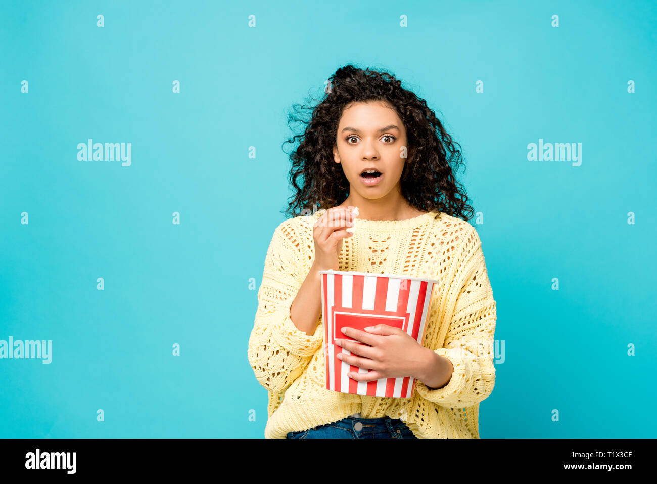 shocked curly african american girl eating popcorn isolated on blue ...