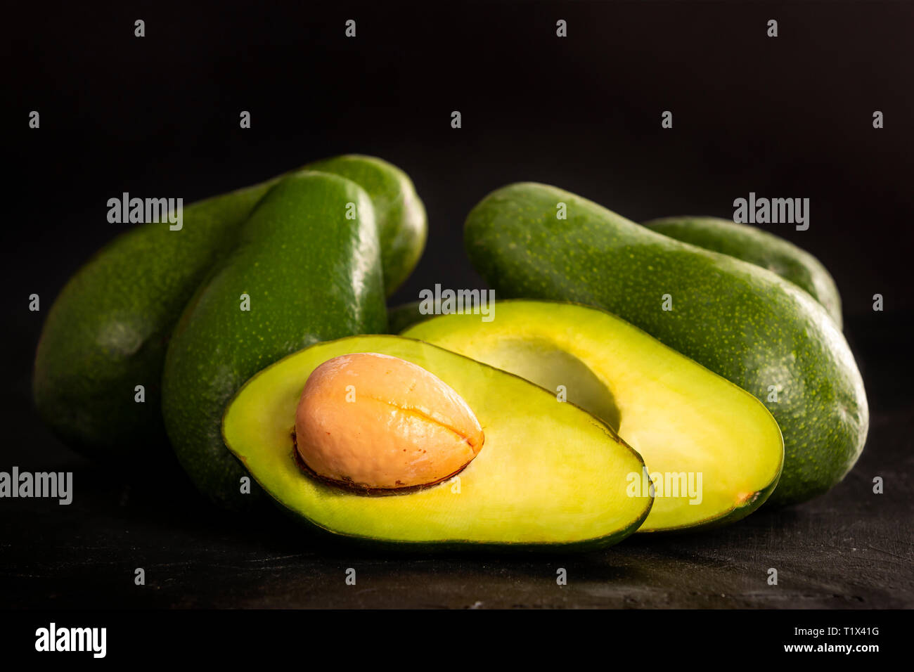 Pile of whole and cut ripe avocados placed on shabby timber tabletop ...