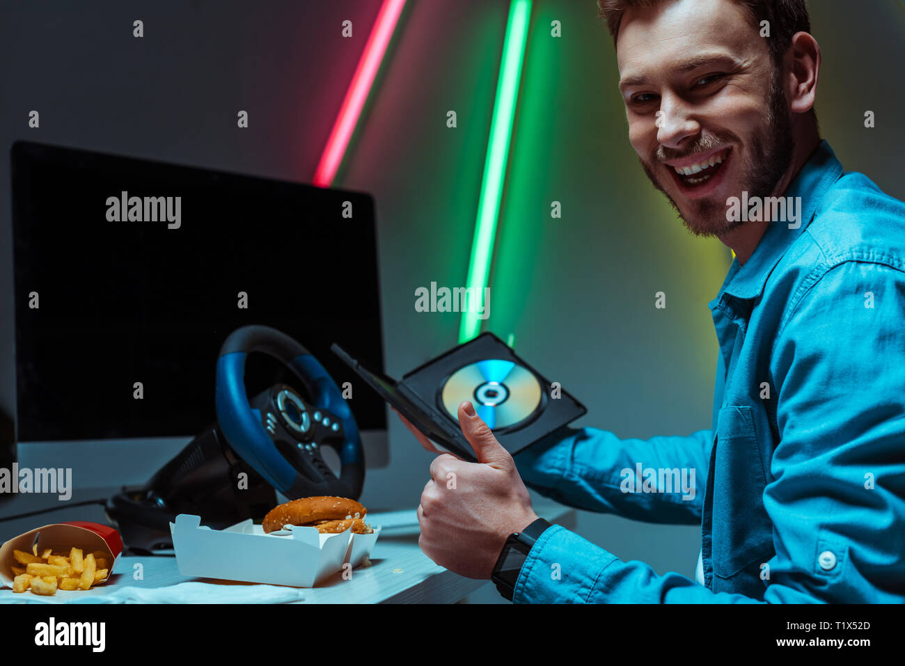 handsome and smiling man holding compact disk with video game and ...