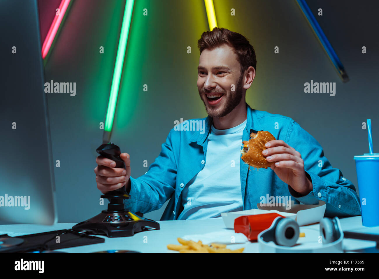 handsome and smiling man holding tasty burger and playing video game ...