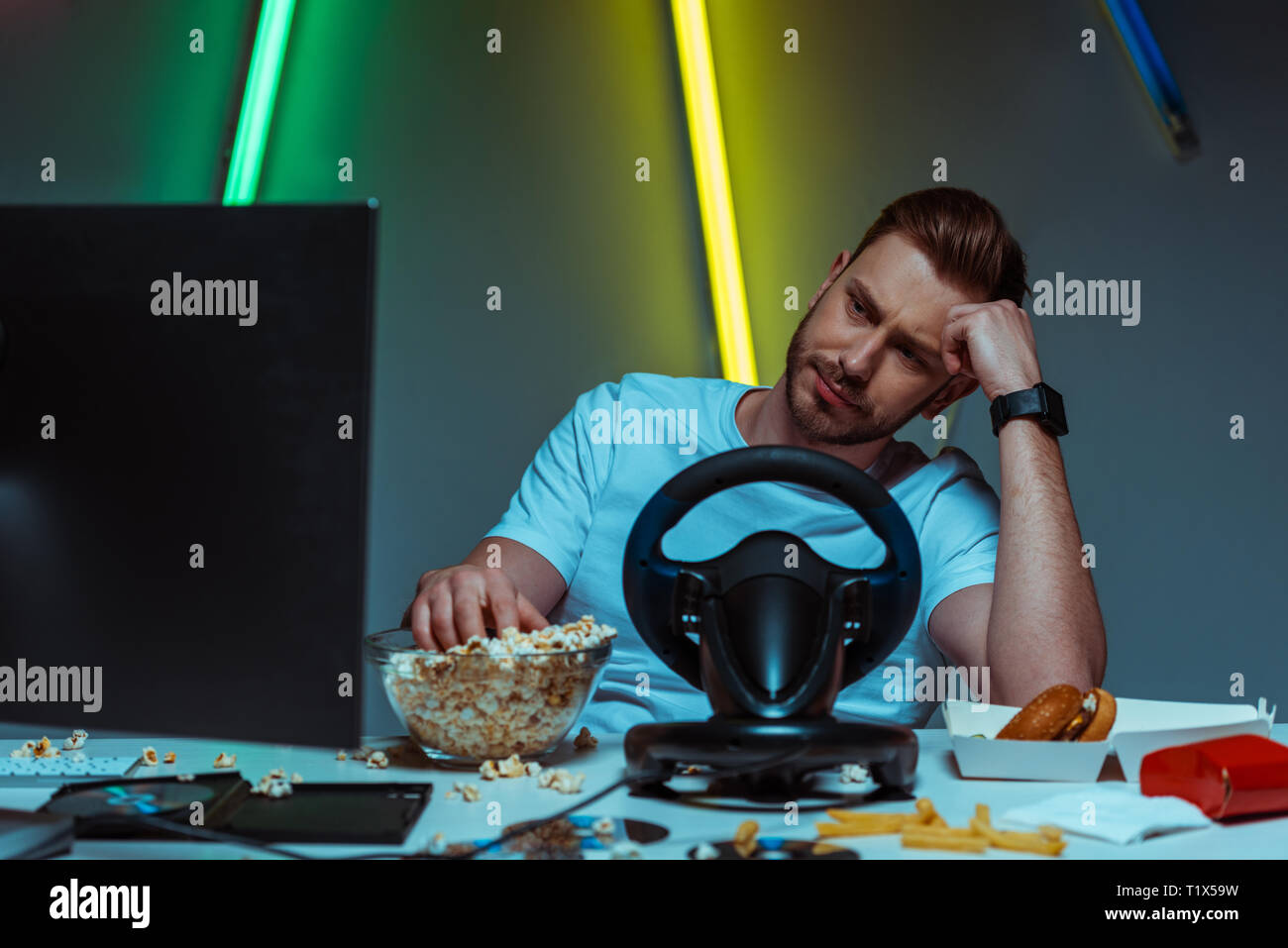 handsome and sad man looking at computer monitor and eating popcorn ...