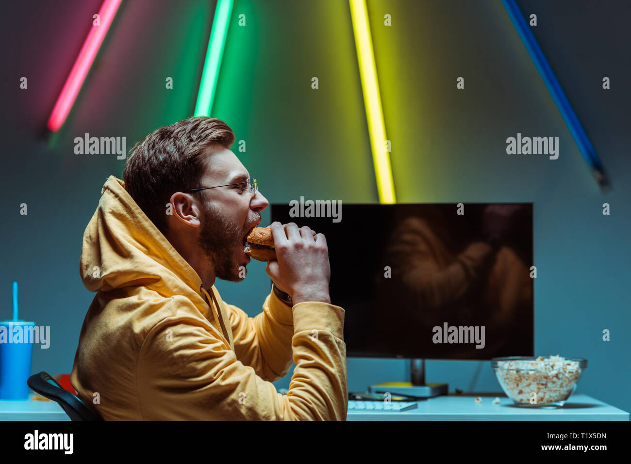 side view of handsome and young adult man eating tasty burger and ...