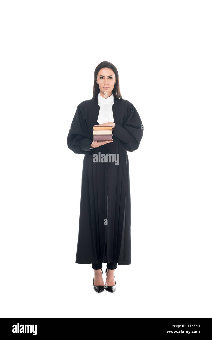 Full length view of serious judge in judicial robe holding books ...