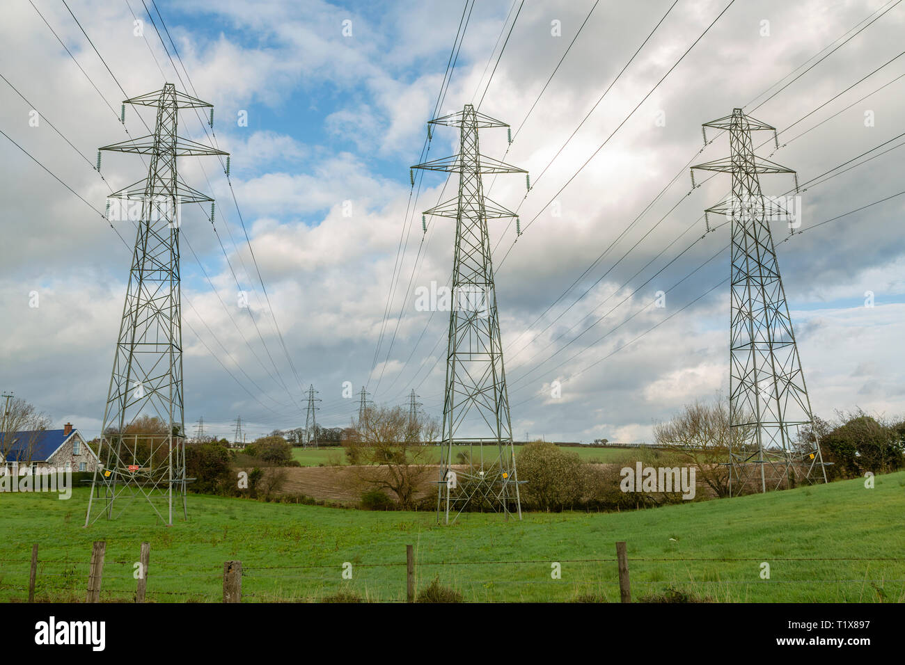 Set of three electric pylons carrying cables set against a part cloudy ...