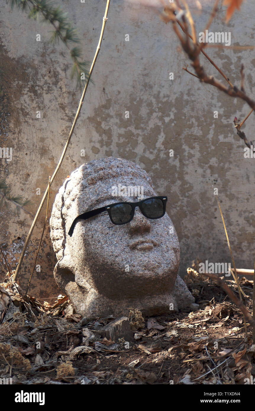 The head of a broken statue with dark glasses by the concrete wall ...